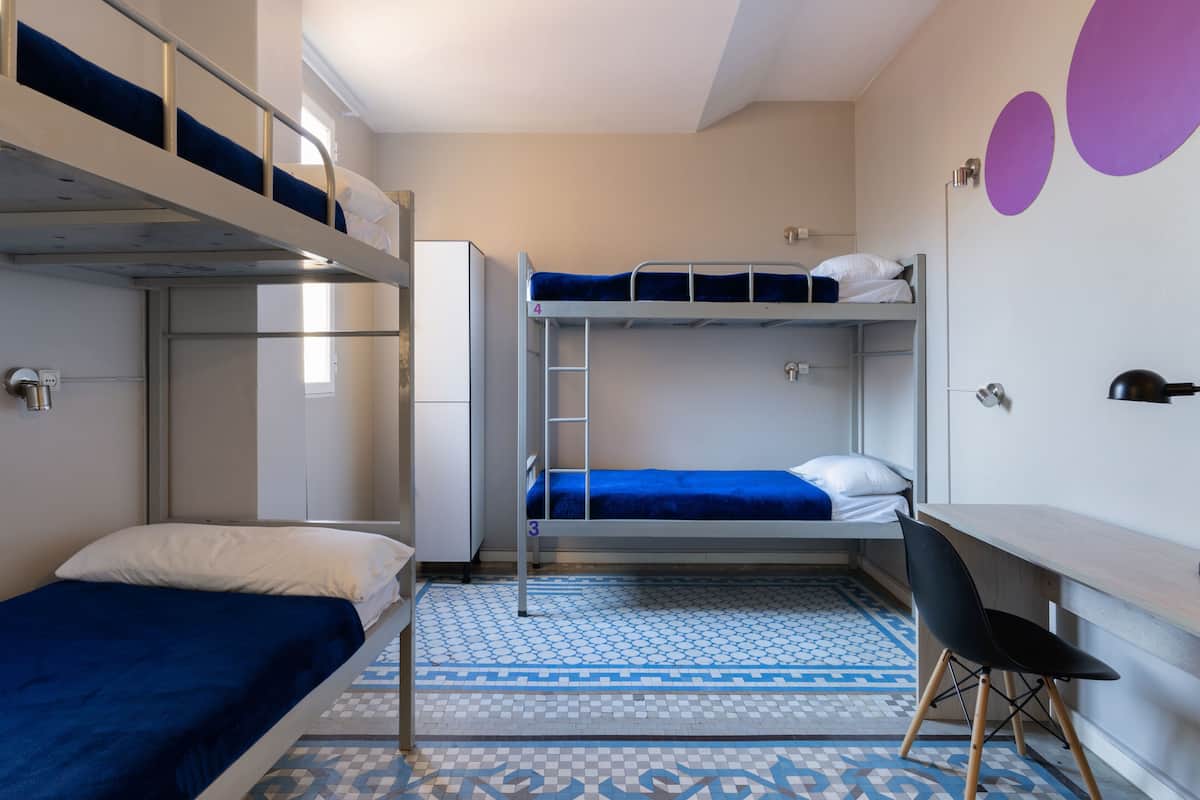 Quarto em dormitório com beliches, uma mesa e uma cadeira.