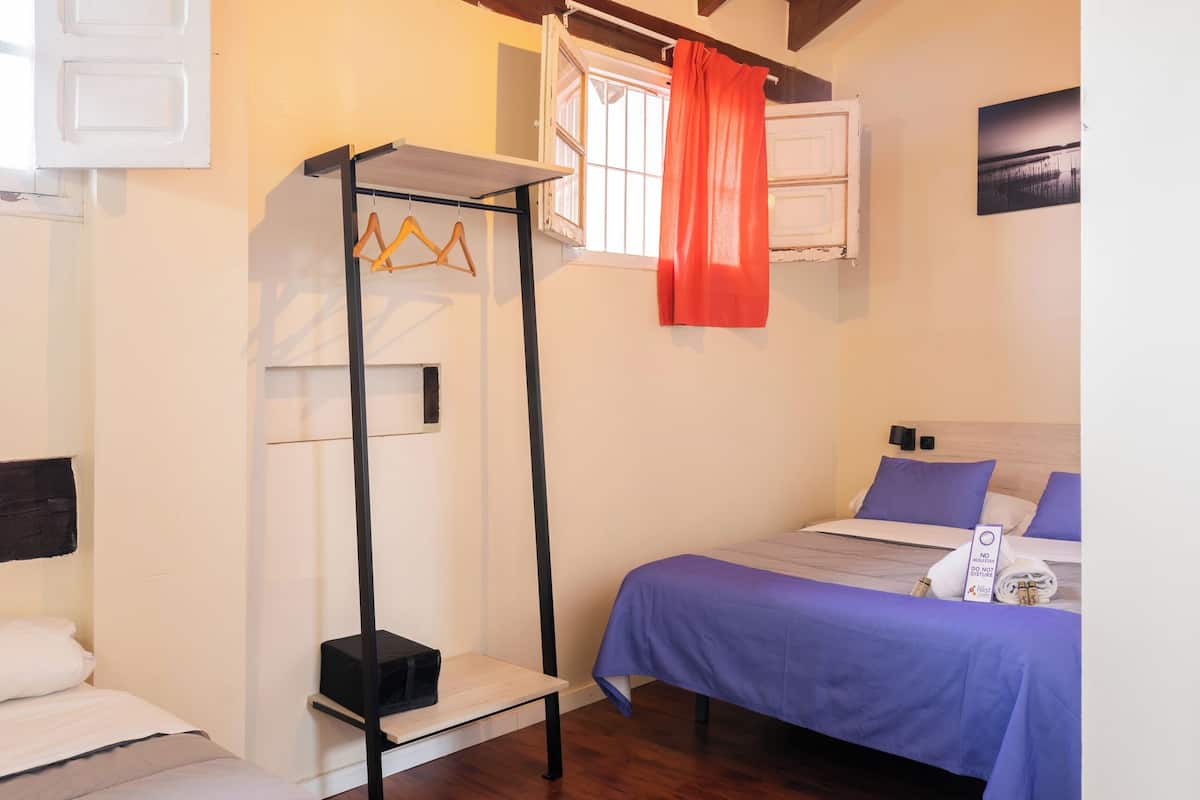 Quarto com duas camas, piso de madeira, um guarda-roupa e teto com vigas aparentes.