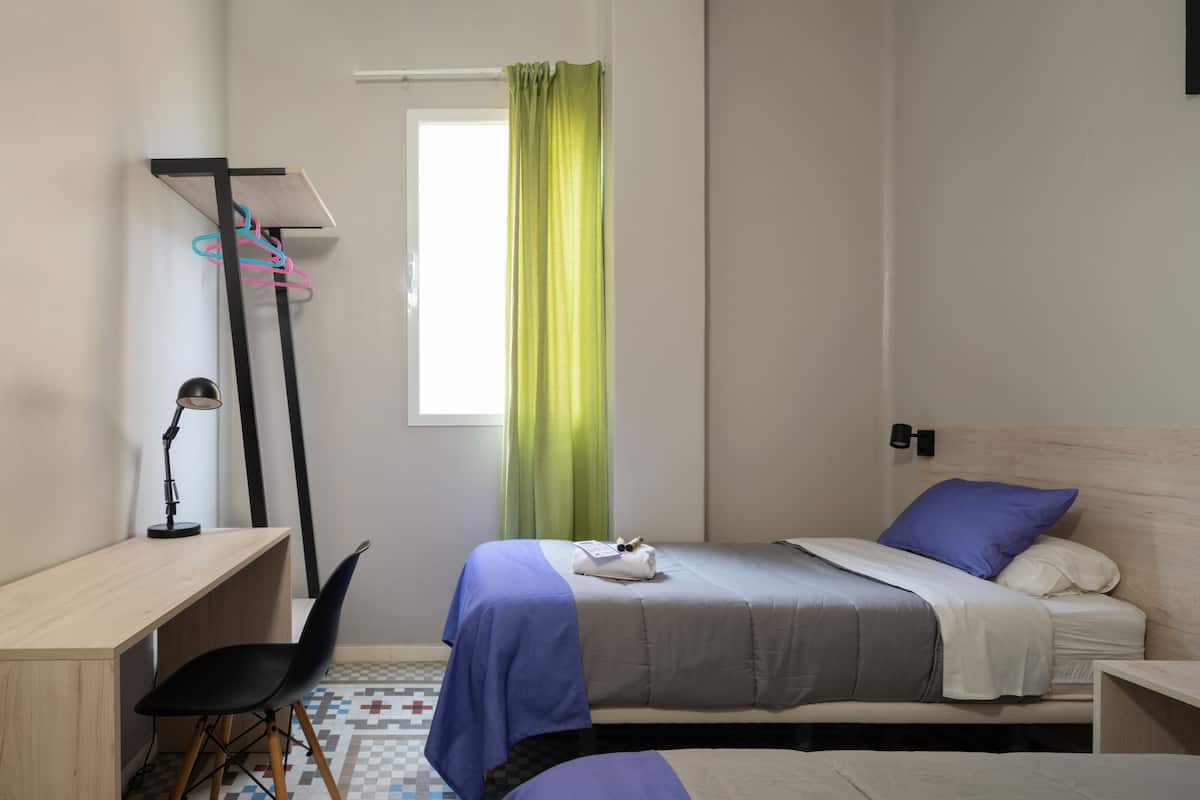 Quarto pequeno com cama, escrivaninha e cadeira.