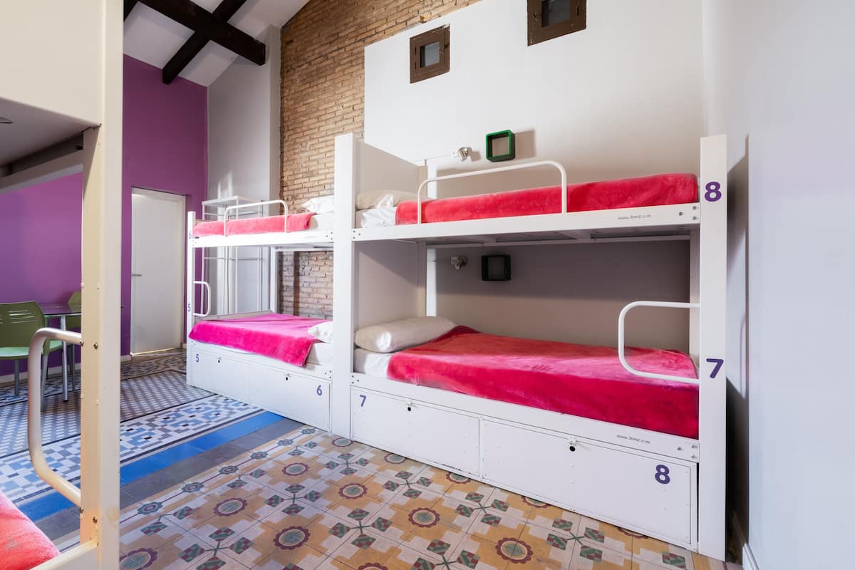 Quarto tipo dormitório com beliches numerados de 6 a 8, piso estampado e parede de tijolos.