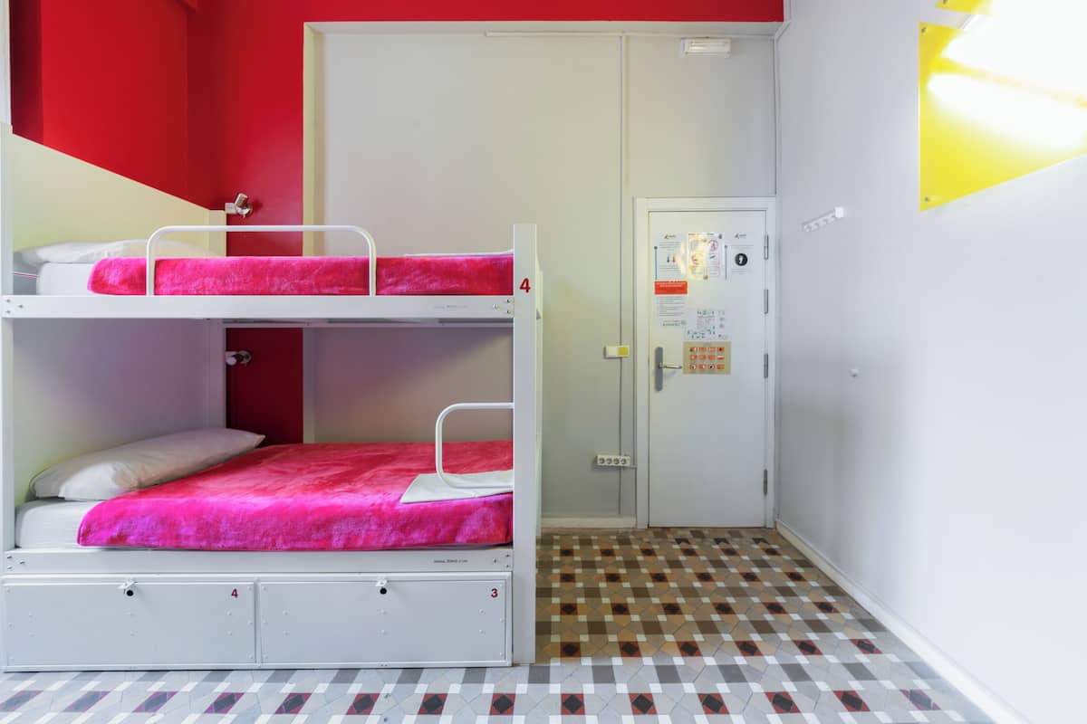 Um dormitório com beliches, uma porta com um mural de avisos e um chão estampado.