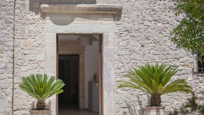 Um edifício de pedra com uma porta de entrada que dá para um espaço interior. Há duas plantas em vasos com folhagem verde em frente à porta.