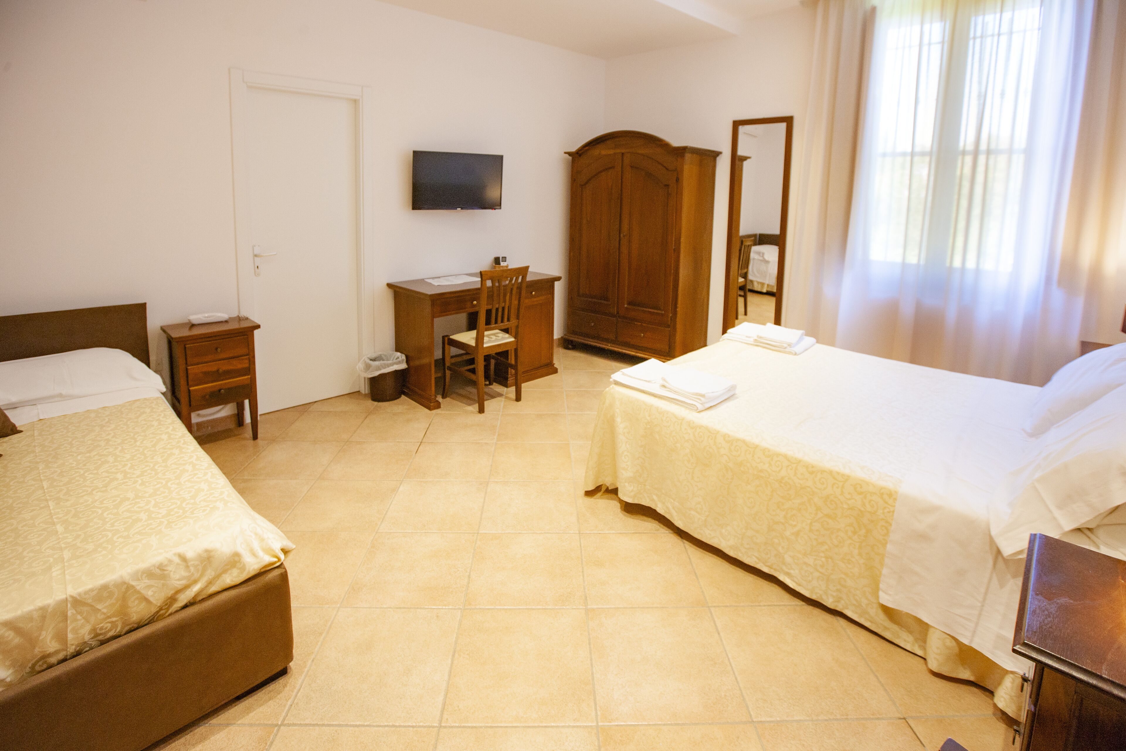 Quarto de hotel com duas camas, uma escrivaninha, um guarda-roupa, uma televisão e um espelho.
