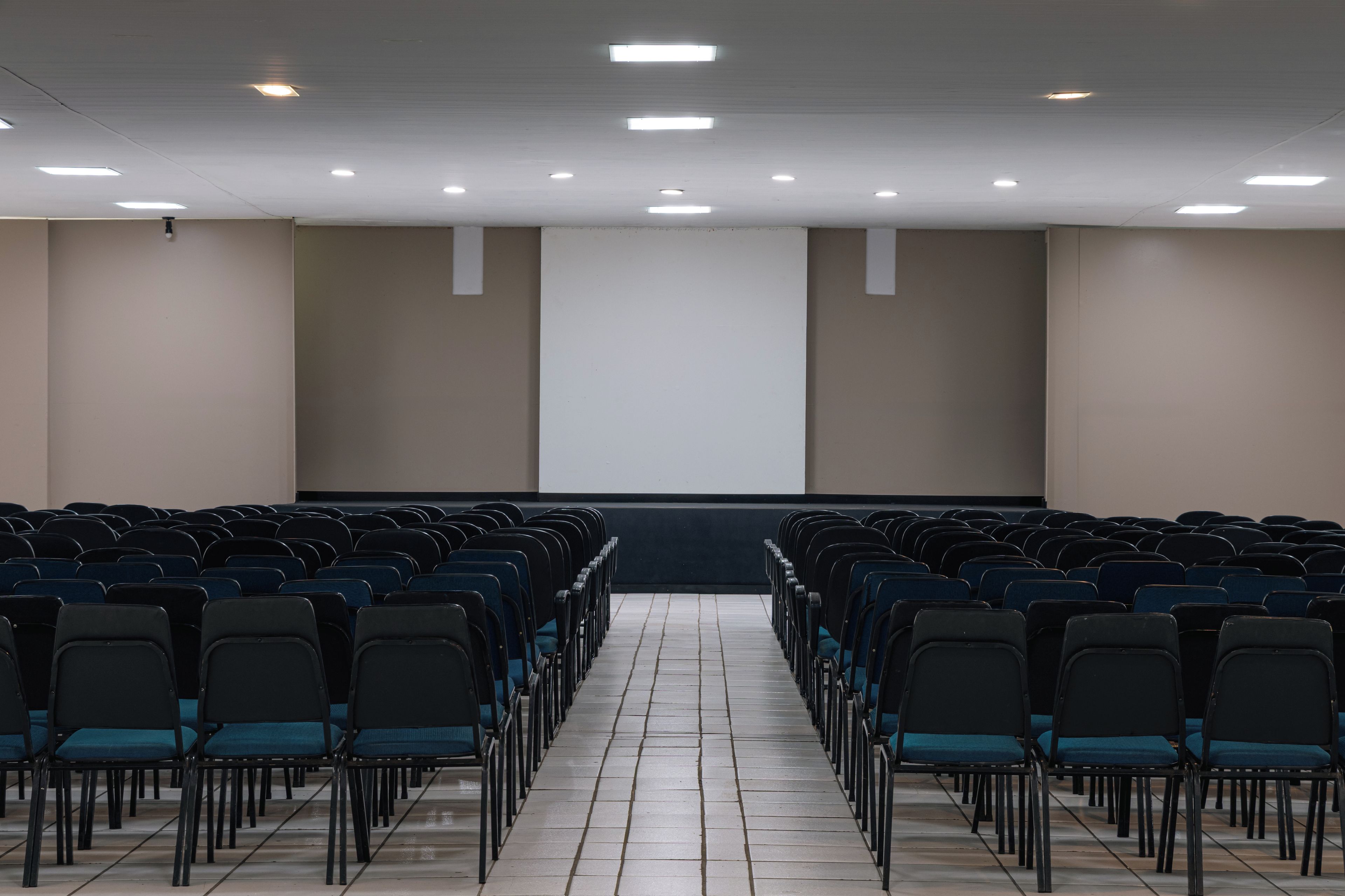 Sala de conferência com fileiras de cadeiras voltadas para uma tela de projeção grande.
