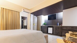 Quarto de hotel com uma cama grande, uma pequena cozinha e uma área de refeições com cadeiras.