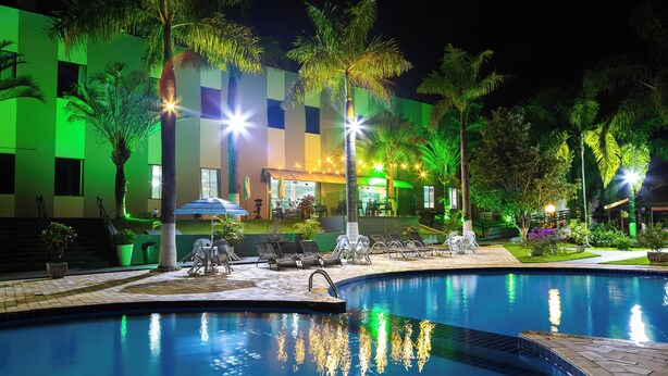 Área de piscina à noite, com espreguiçadeiras e um edifício ao fundo.