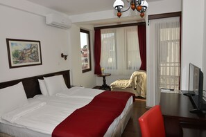 Quarto de hotel com uma cama grande, uma escrivaninha com computador, uma cadeira, uma mesinha de centro com um vaso e um quadro na parede.