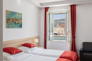 Quarto de hotel com duas camas, um quadro na parede, janela com vista para a paisagem urbana e uma cadeira.