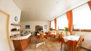 Uma sala de jantar com bar, mesas, cadeiras e cozinha equipada com frigorífico.