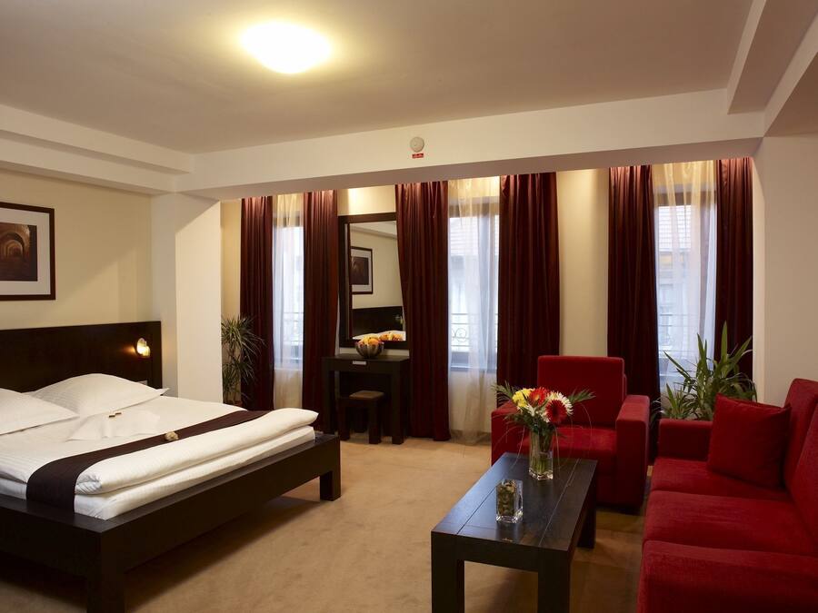 Quarto de hotel com cama, escrivaninha, sofá vermelho e mesa de centro.