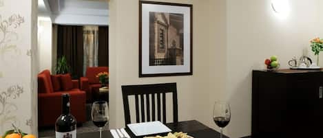 Uma área de refeições com uma mesa posta para dois, uma garrafa de vinho e uma cesta de frutas.