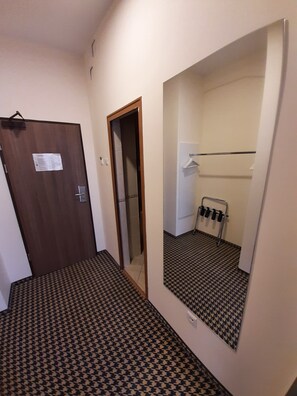 Um corredor com piso estampado, uma porta de madeira com um aviso e um espelho refletindo um porta-toalhas e um armário branco.