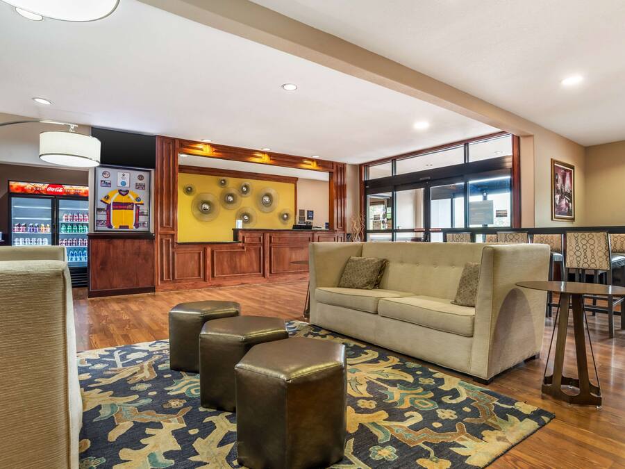 Um saguão de hotel com um sofá, pufes, um tapete estampado, um balcão de recepção, um frigorífico e uma máquina de vendas.