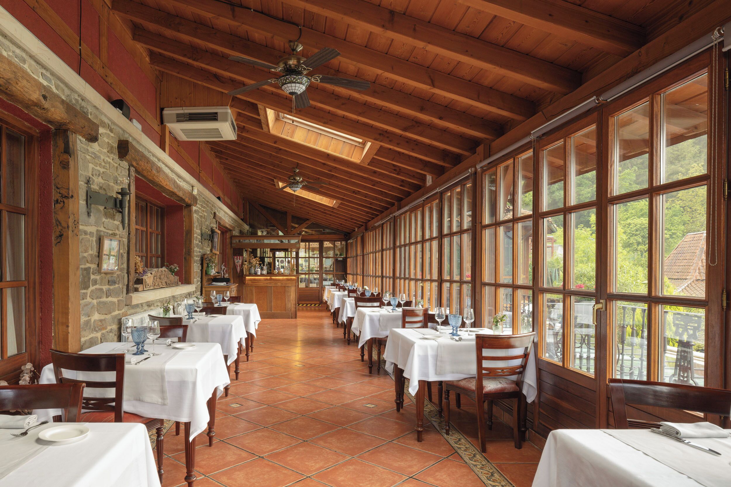 Um restaurante com vigas de madeira, janelas amplas e mesas preparadas para refeições.