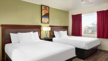 Quarto de hotel com duas camas, uma mesa de cabeceira com abajur, um quadro na parede e uma janela com cortinas vermelhas.