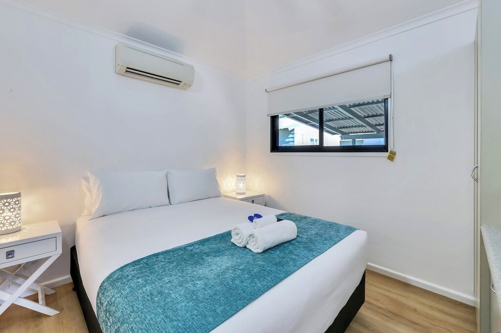 Quarto de hotel com cama, mesa de cabeceira com abajur, janela com vista e aparelho de ar condicionado.