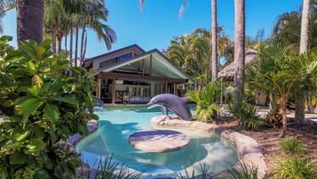 Um edifício moderno com piscina, rodeado por palmeiras e plantas tropicais.