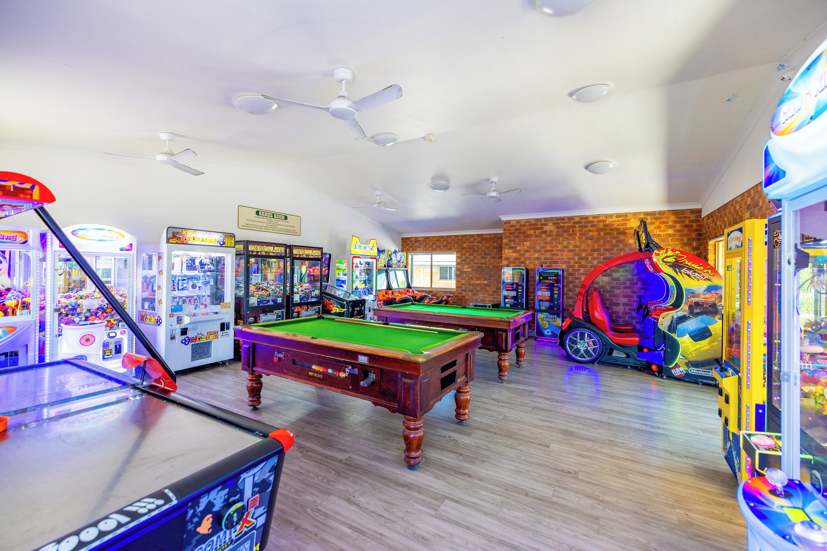 Uma sala com mesas de bilhar, jogos de fliperama e ventiladores de teto.