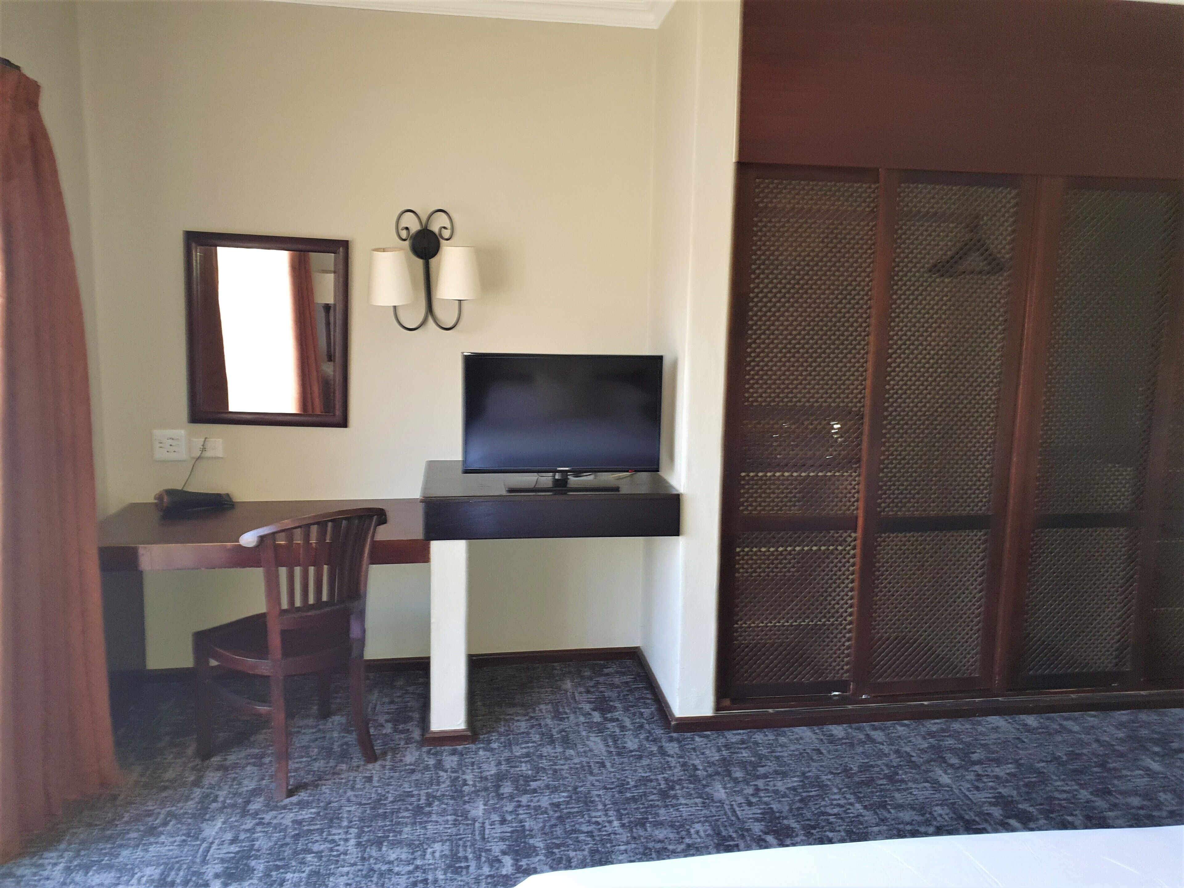 Quarto de hotel com escrivaninha, cadeira, televisão e uma grande porta deslizante.