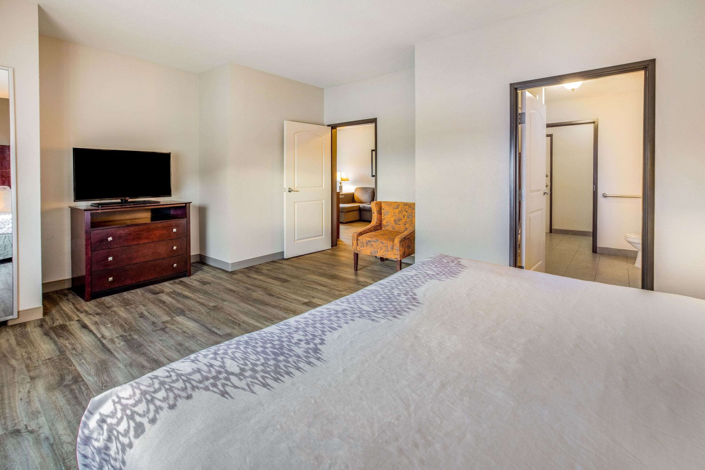 Quarto de hotel com uma cama grande, cômoda com televisão de tela plana, tapete estampado e uma cadeira.