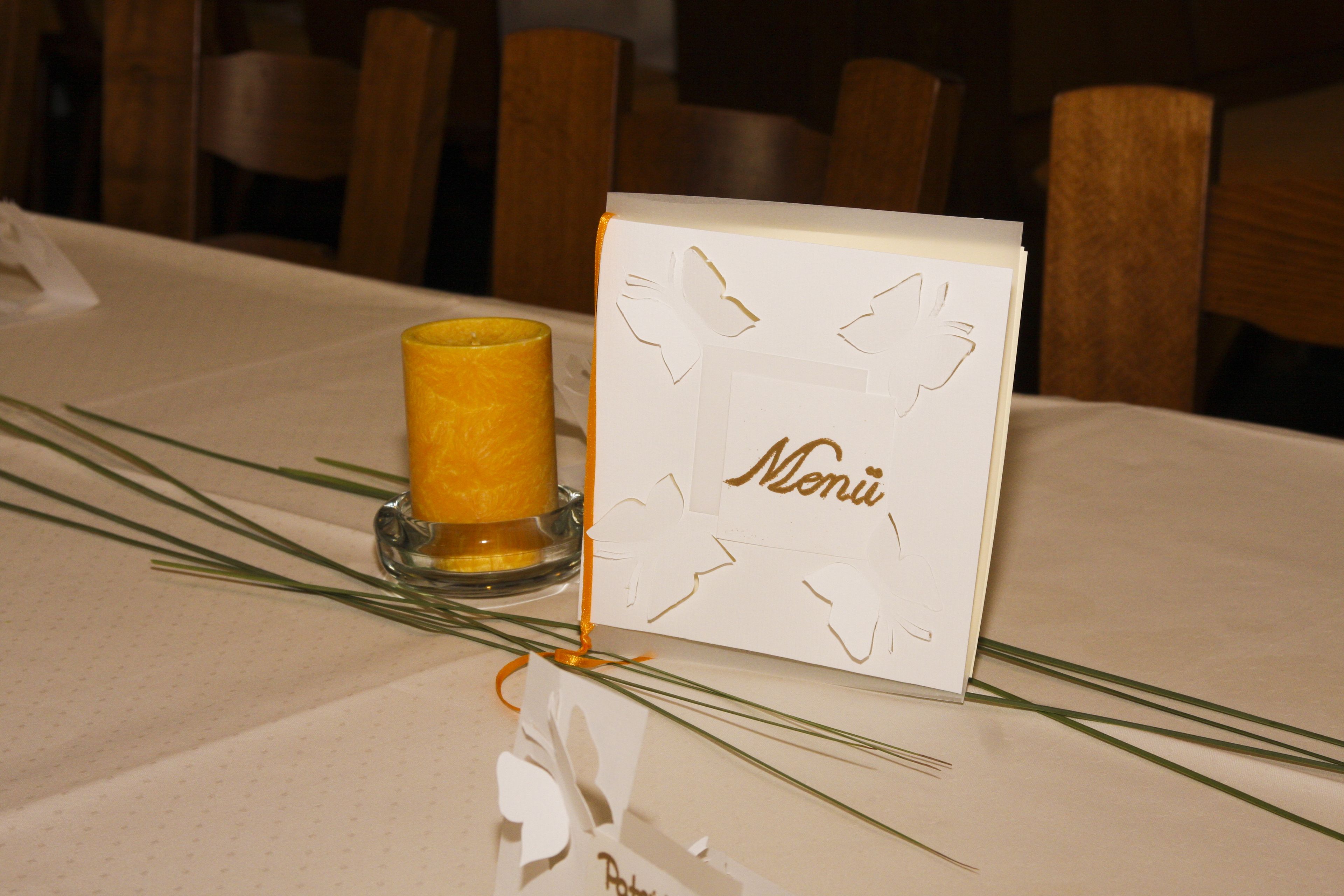 Uma mesa com um cardápio, uma vela e alguns elementos verdes.