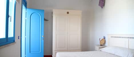 Um quarto com uma cama, um guarda-roupa, uma mesa de cabeceira e uma janela.