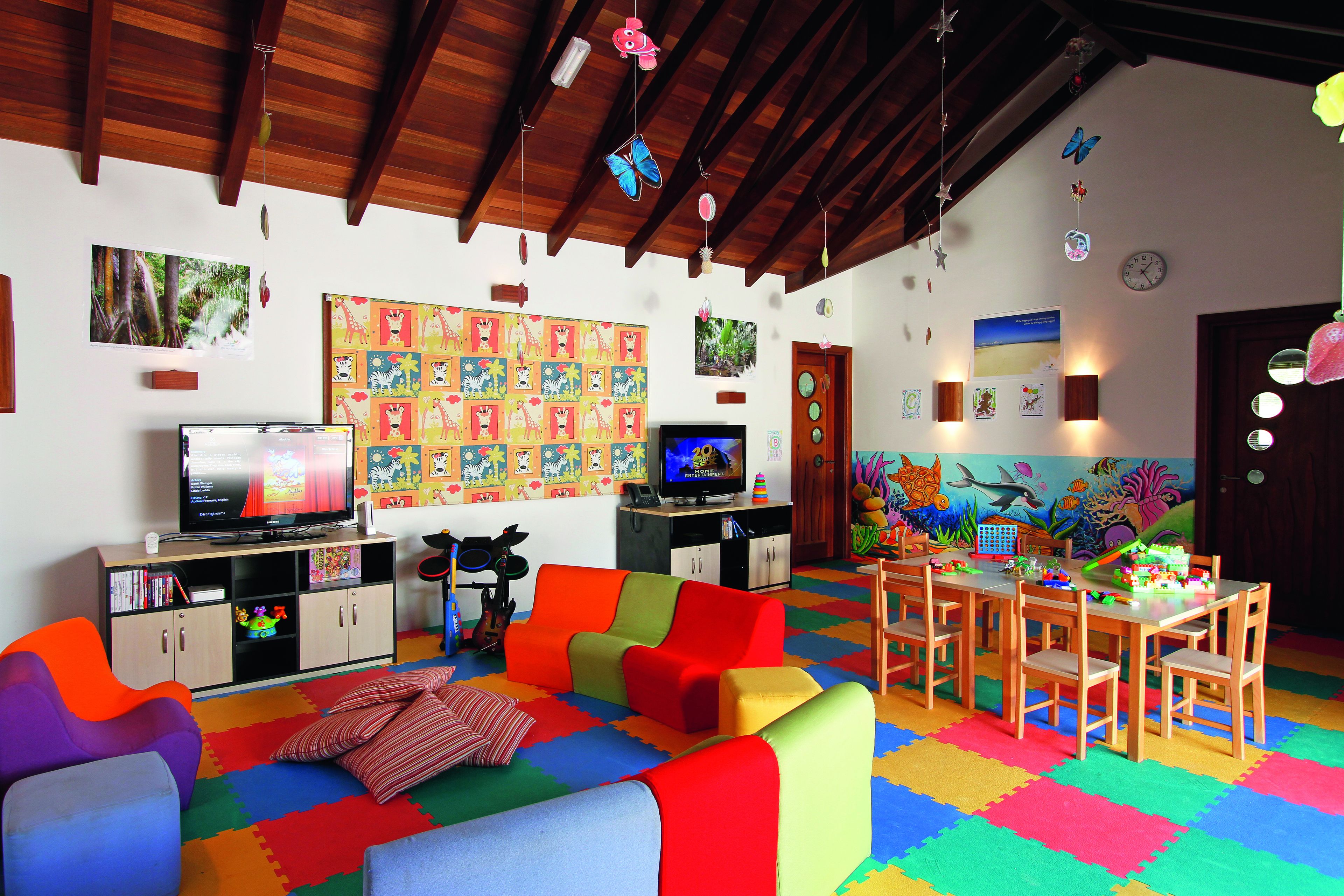 Uma sala de estar acolhedora com móveis coloridos, uma televisão e um mural vibrante na parede.