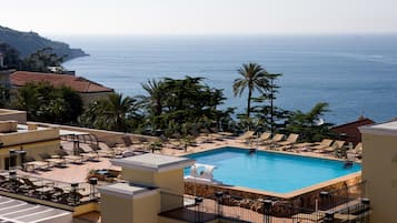 Piscina no terraço com espreguiçadeiras e palmeiras, com vista para a costa.