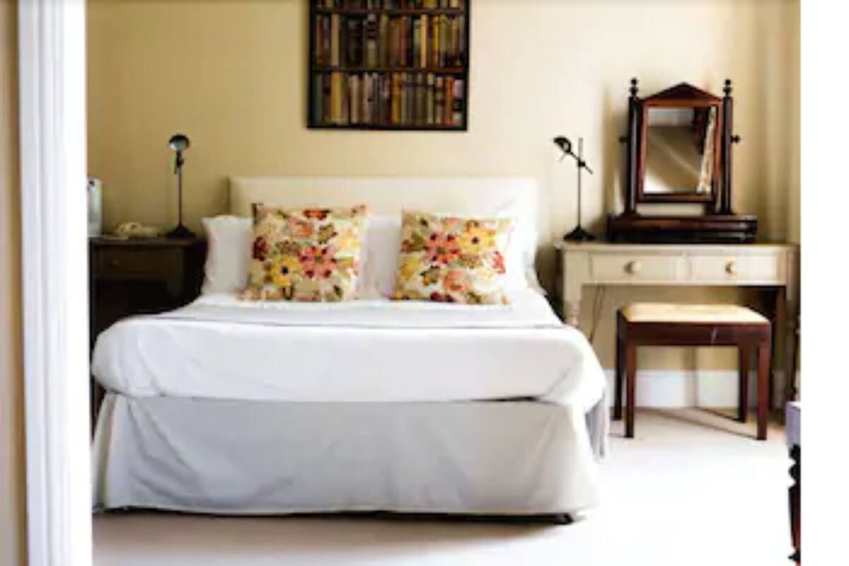 Quarto bem organizado com cama, mesa de cabeceira, cadeira, escrivaninha e estante.