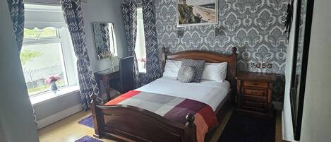 Quarto com cama, mesa de cabeceira, janela com cortinas, quadro na parede e porta com puxador.