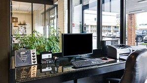 Balcão de recepção com computador, impressora e planta.