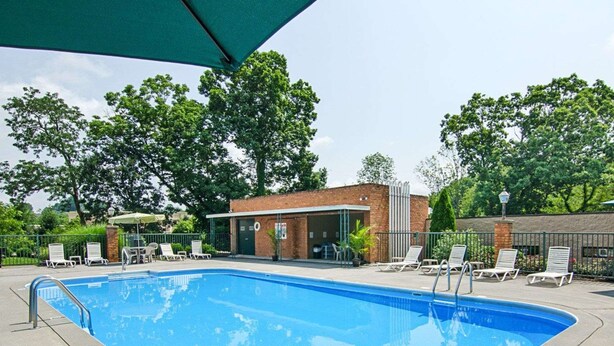 Piscina com espreguiçadeiras e um prédio de tijolos ao fundo.