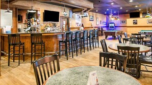 Uma área de bar com banquetas de madeira, mesa de bilhar e mesa de sinuca.