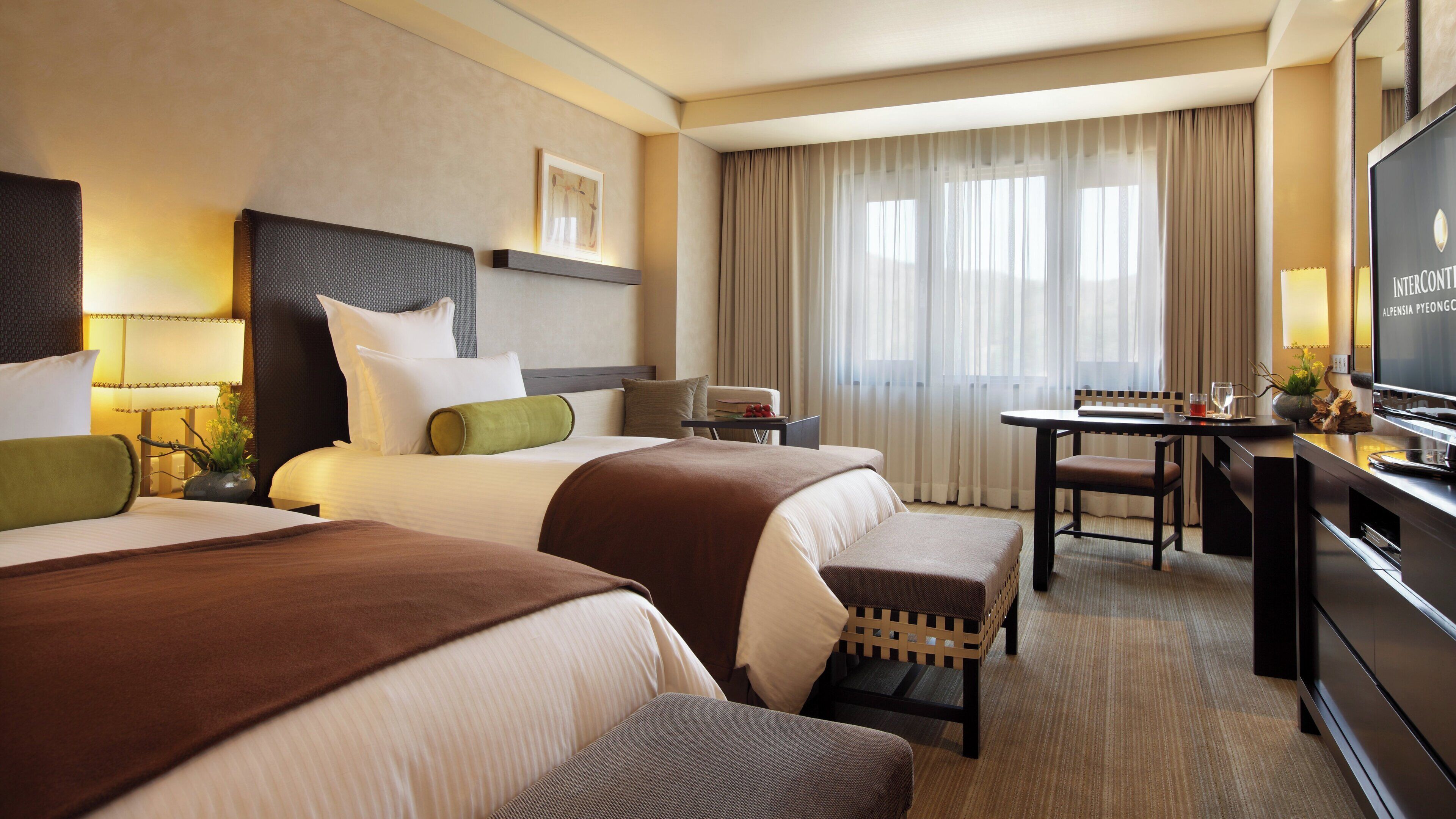 Quarto de hotel com duas camas, uma escrivaninha e uma televisão.