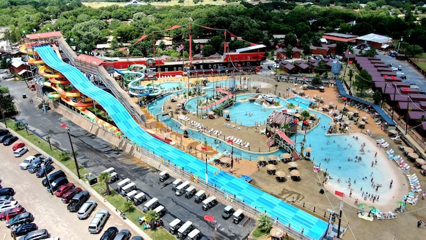 Parque aquático com vários toboáguas e piscinas, estacionamento e área de praia.