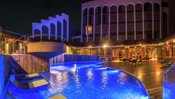 Uma área de piscina noturna com design moderno, incluindo uma fonte original e um espaço com assentos.