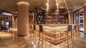 Uma área de bar moderna com mobiliário de madeira, um balcão central e uma variedade de garrafas de bebidas.