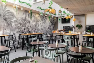 Interior de restaurante com várias mesas e cadeiras, um balcão de bar e um mural de paisagem tropical.