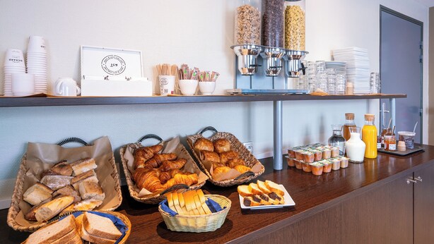 Buffet de café da manhã com croissants, pães, doces e diversas bebidas.