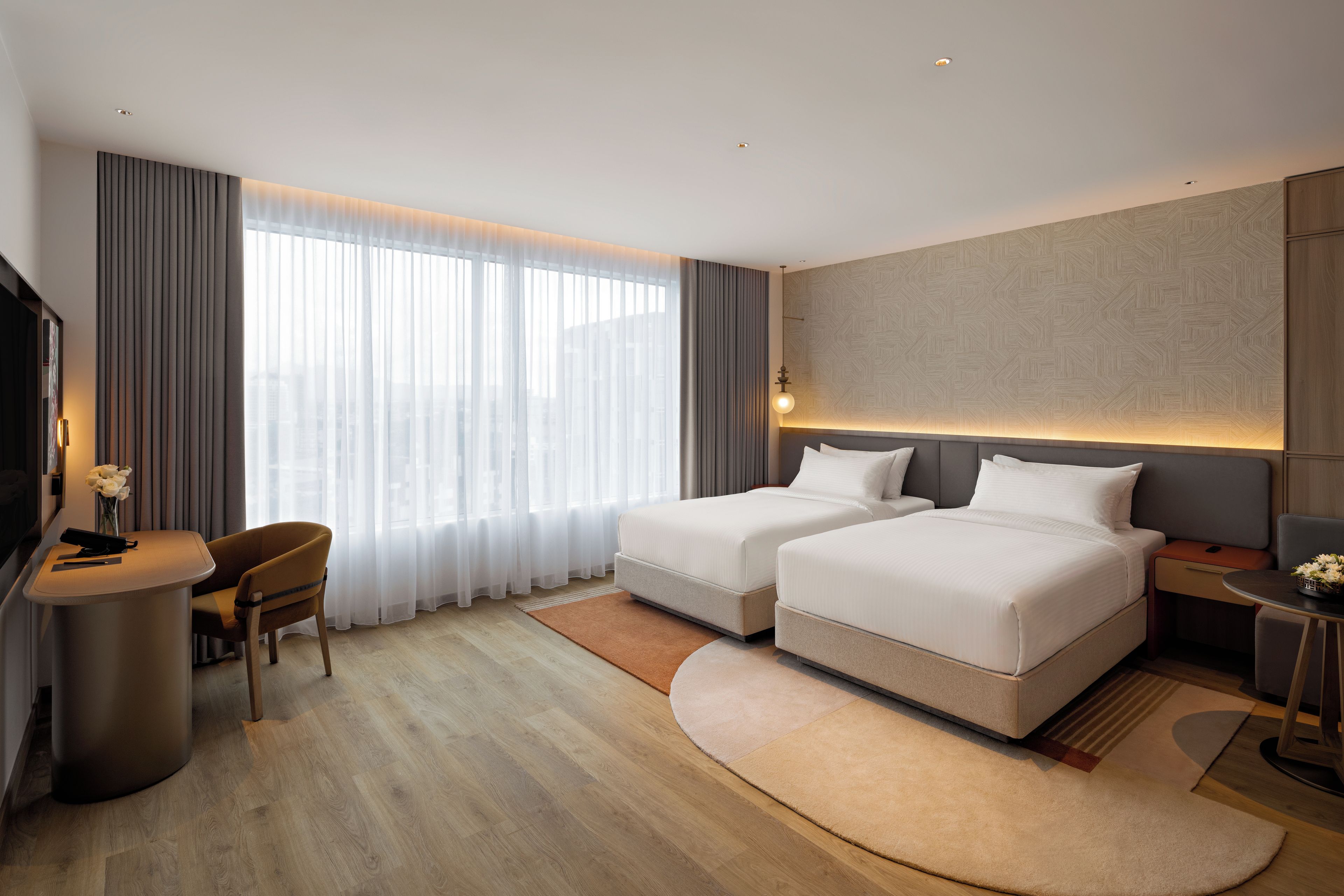 Quarto de hotel com duas camas, uma escrivaninha, uma cadeira, televisão e uma janela grande com cortinas.