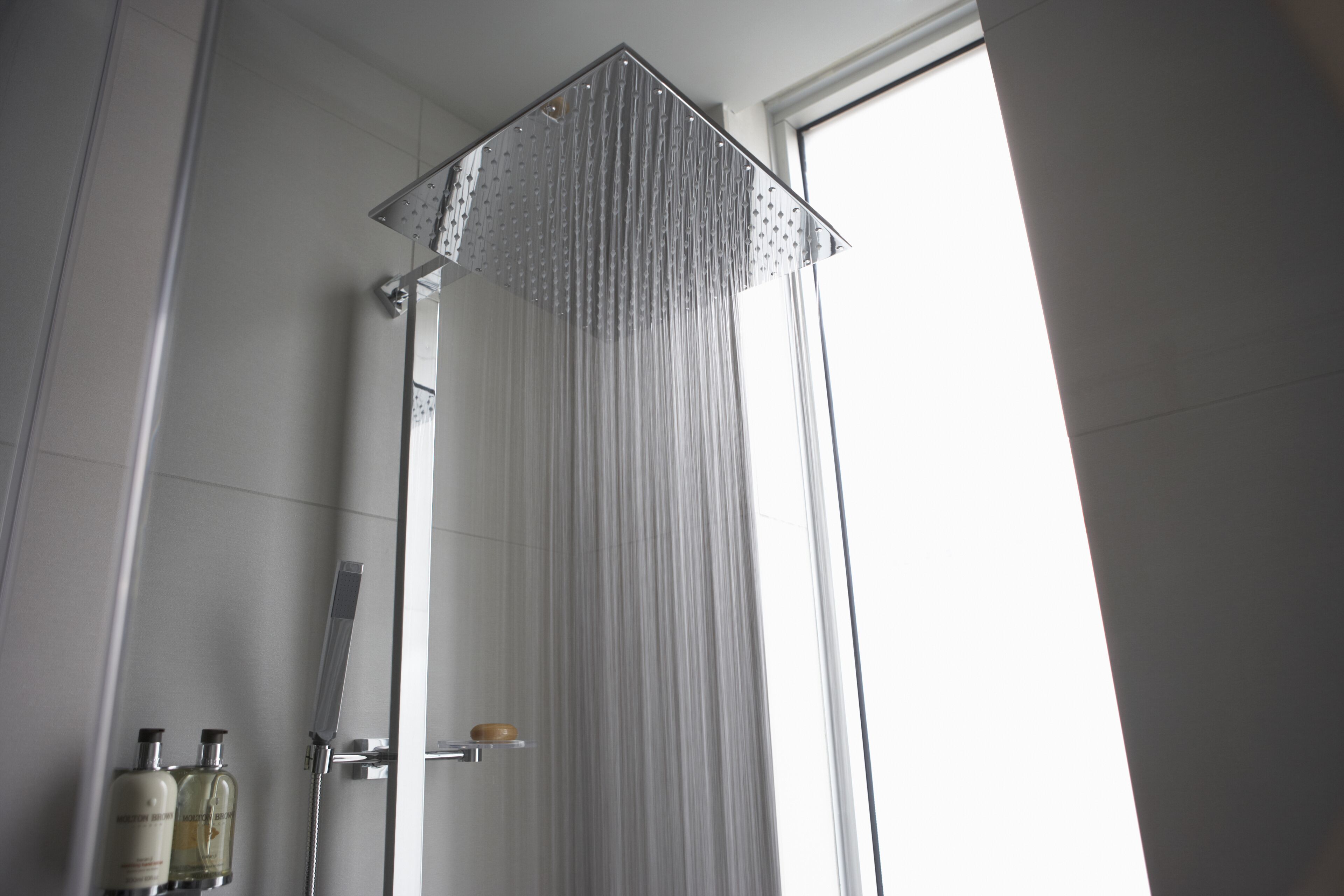 Um chuveiro moderno com função de queda de chuva, um chuveiro manual e duas garrafas de shampoo em uma prateleira.