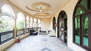 Um espaço ao ar livre coberto, com chão de azulejos, assentos e janelas amplas.