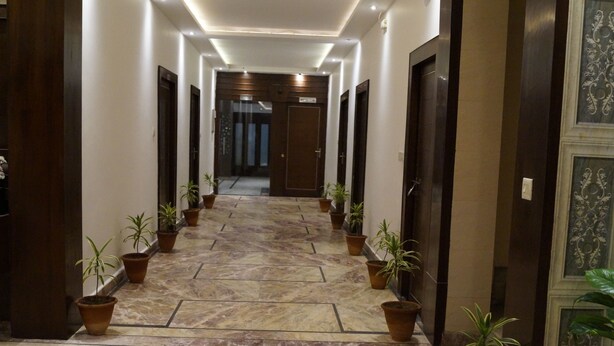 Um corredor com piso de mármore, plantas em vasos e portas que dão para os quartos.
