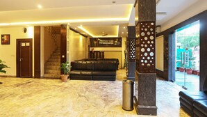 Um hall amplo com piso de mármore, um sofá de couro preto, uma escada e uma grande janela com vista para o exterior.