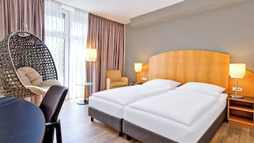 Quarto de hotel com cama, duas cadeiras, uma cadeira suspensa e uma mesa.