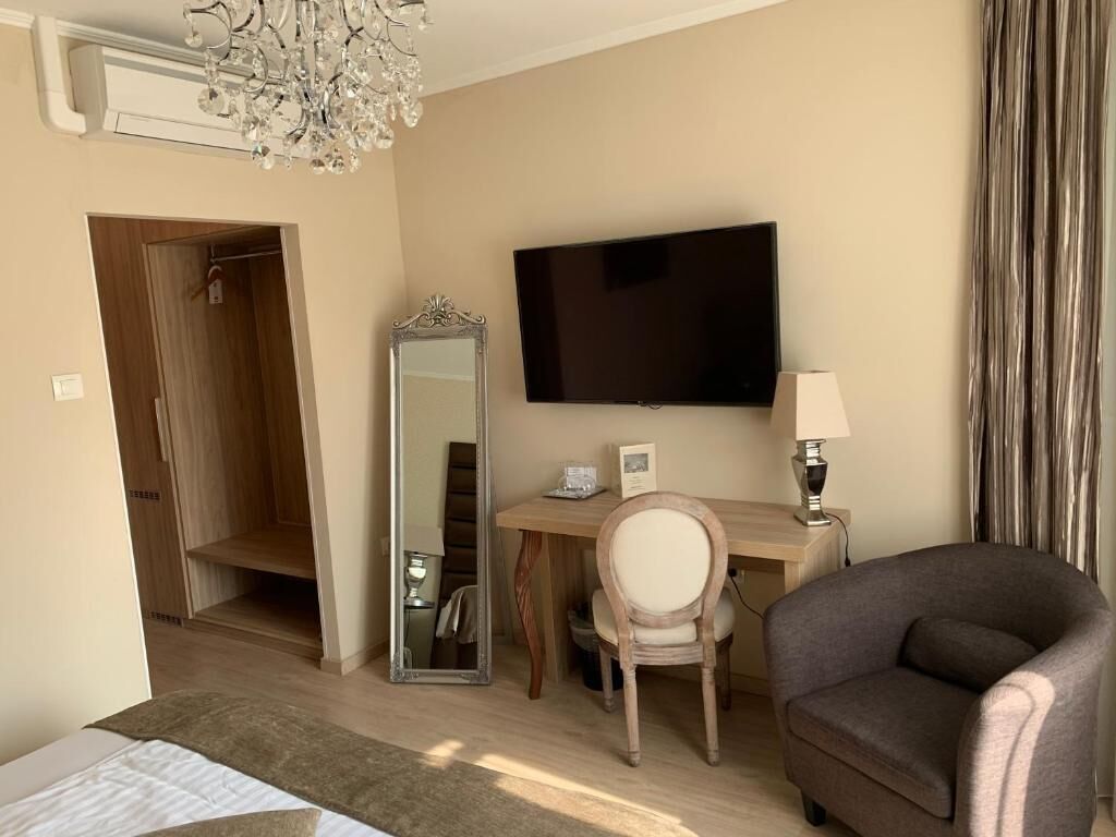 Quarto de hotel com cama, escrivaninha com cadeira, televisão, espelho e lustre.