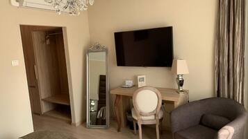 Quarto de hotel com cama, escrivaninha com cadeira, televisão, espelho e lustre.