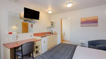 Quarto de hotel com cama, escrivaninha com cadeira, micro-ondas, televisão e um quadro na parede.