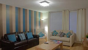 Uma sala de estar com papel de parede listrado, dois sofás com almofadas, uma mesa de centro e um abajur.
