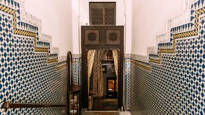 Um corredor estreito com paredes de azulejos estampados e uma porta de madeira com desenhos elaborados.